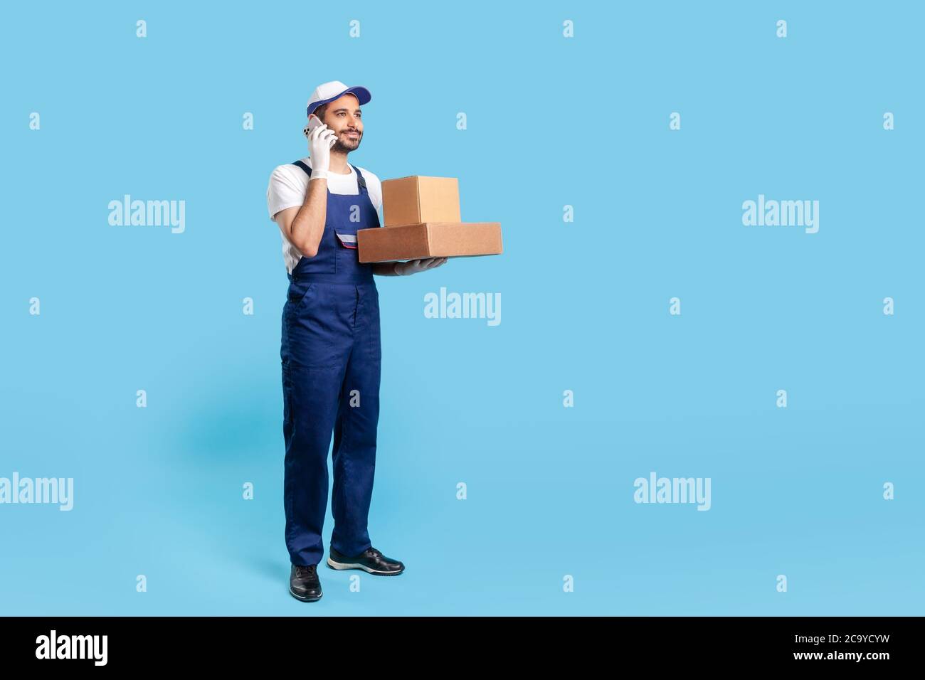 Full length happy friendly delivery man in uniform talking on cellphone ...