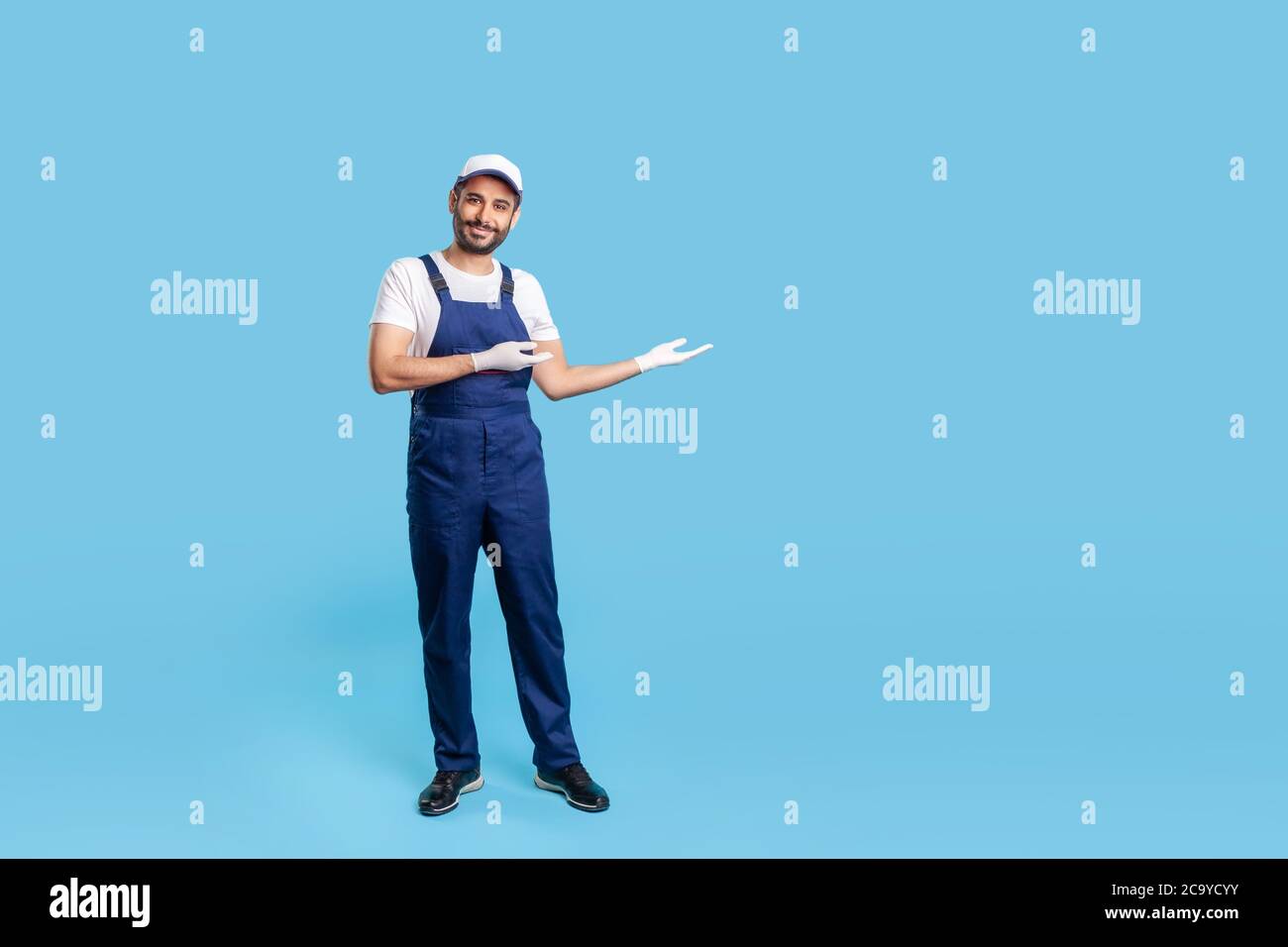 Full length cheerful workman in blue overalls, cap and protective ...