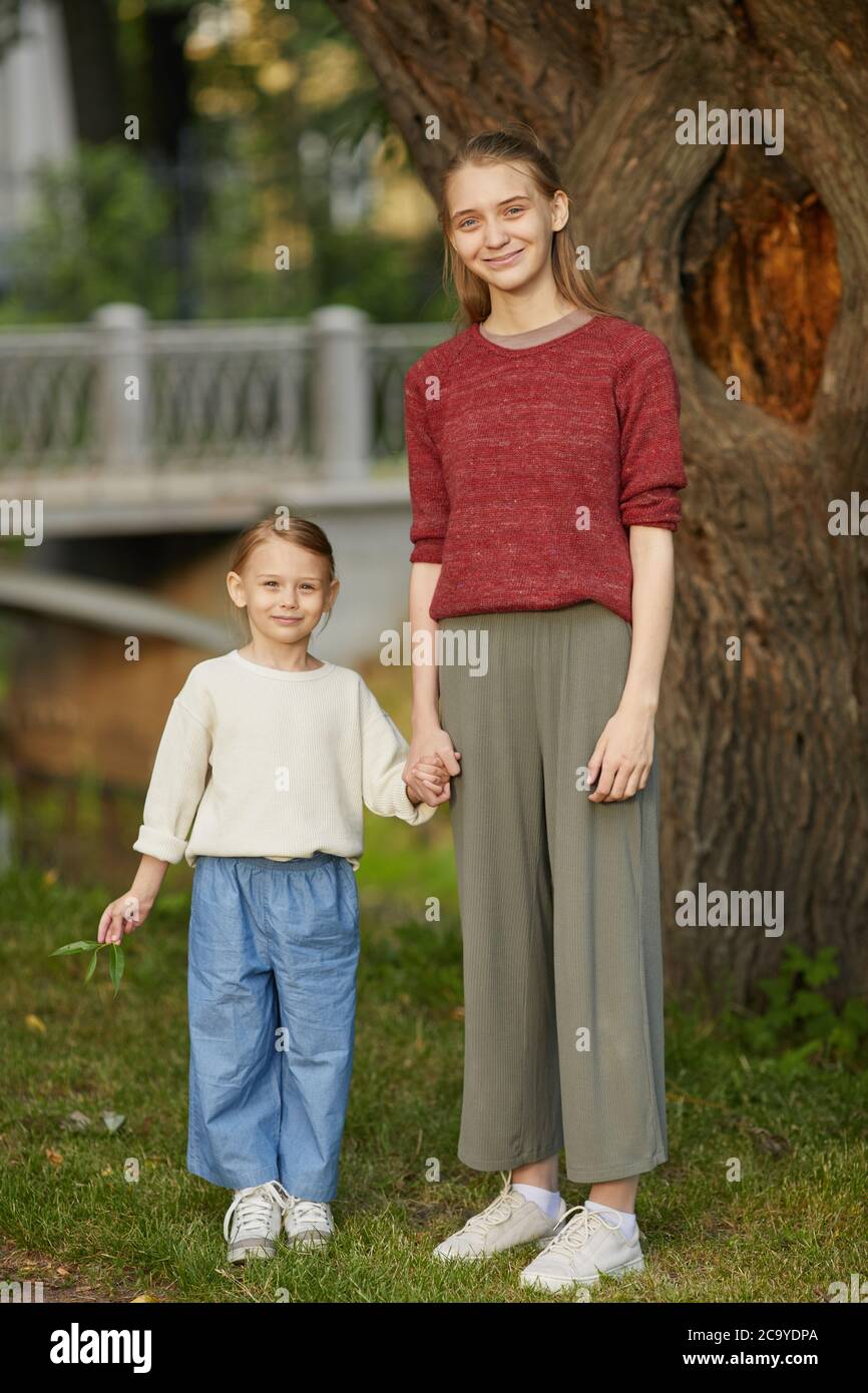 Vertical full length portrait of two sisters holding hands while ...