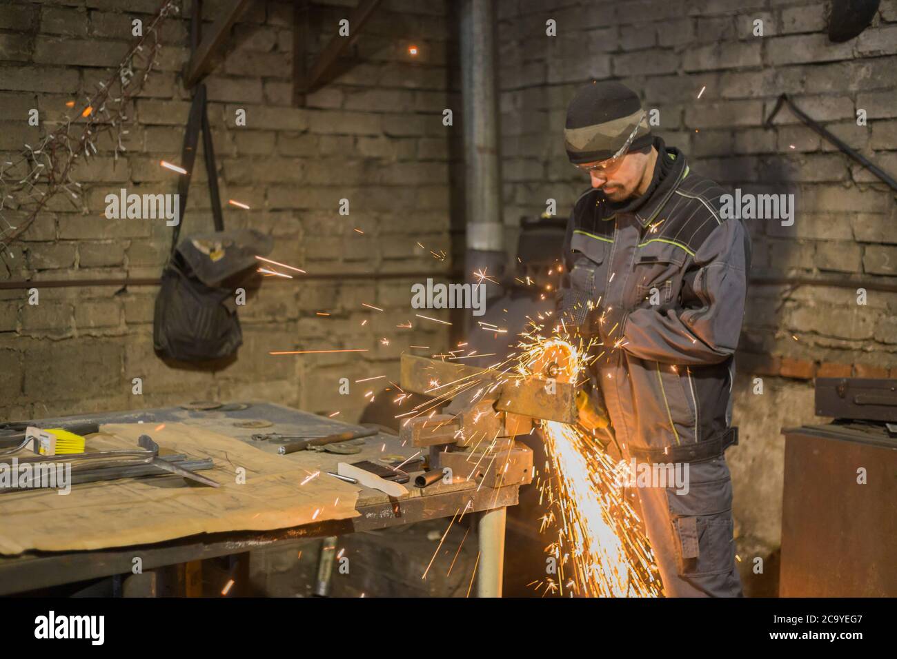 Professional blacksmith sawing metal with hand circular saw at forge ...