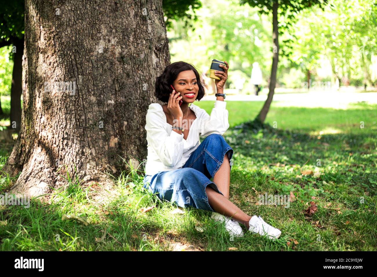 Beautiful african woman talking by phone and sitting on the grass Stock ...