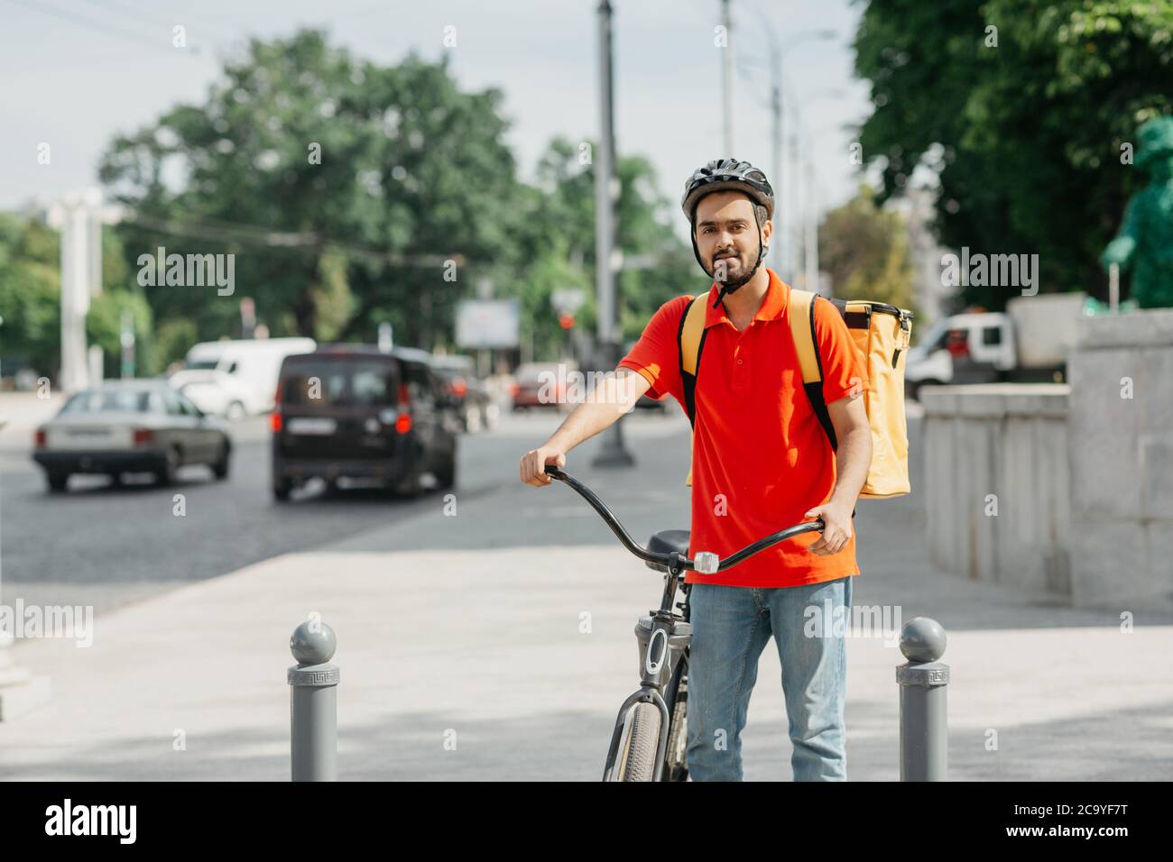 Goods delivery service. Friendly courier in helmet with big bag, stands ...