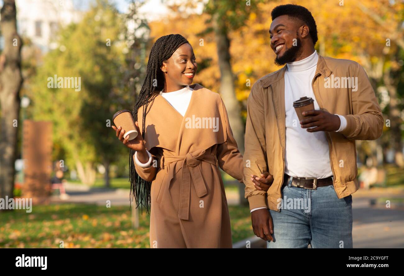 Millennial afro couple walking in autumn park and drinking takeout ...