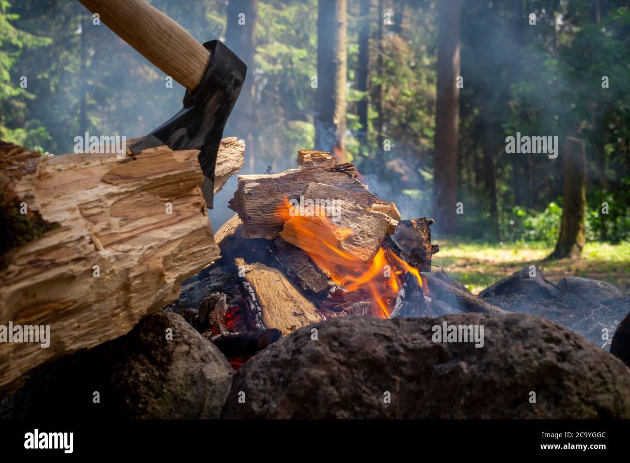 Camp fire in a forest with chopper lodged in a log of wood in the ...