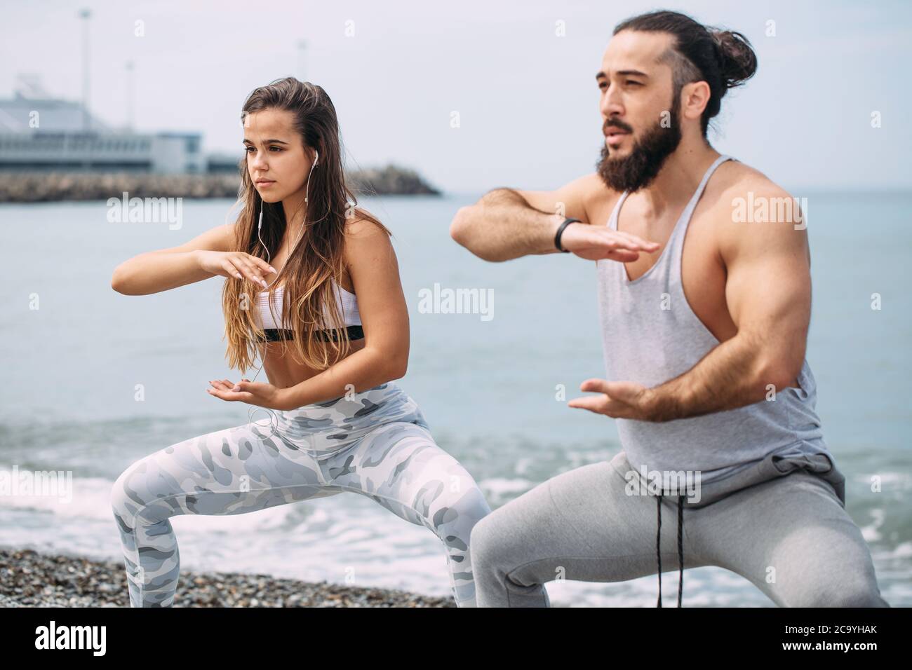 Couple warming out outdoors, doing squats together on the ocean pebble ...