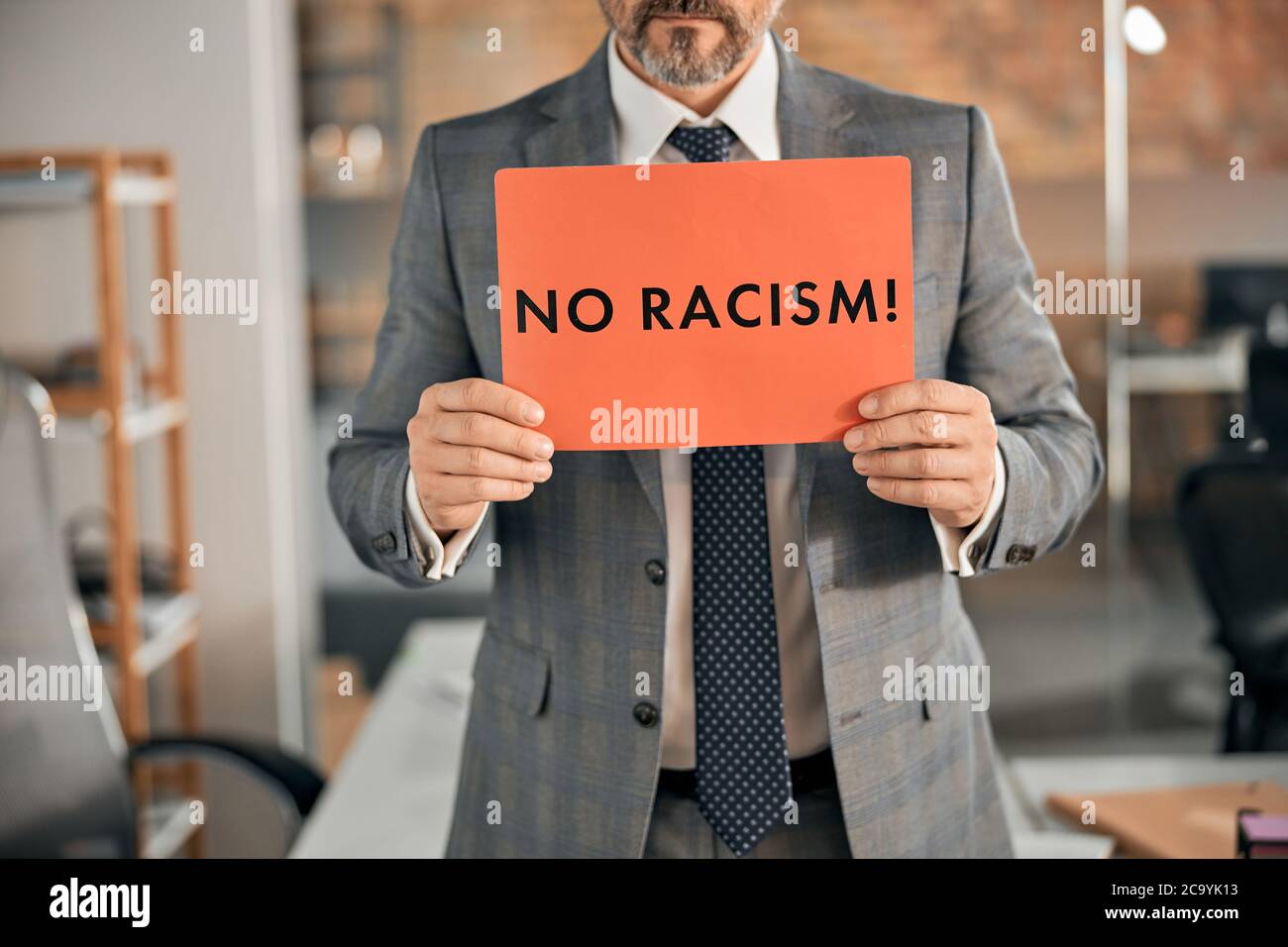 Man in suit holding no racism placard Stock Photo - Alamy