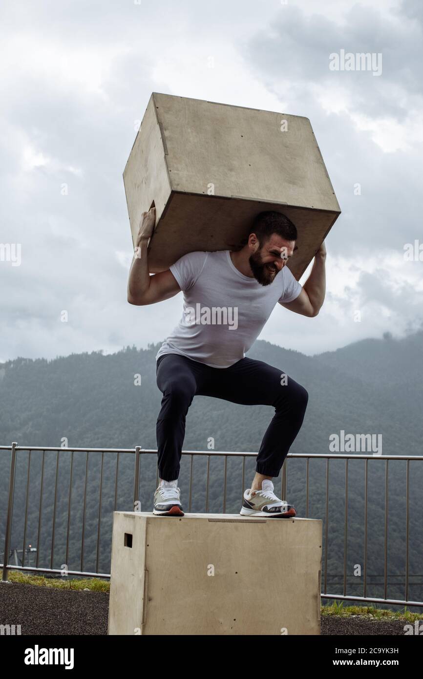 Young bearded athlete doing squats with weightning blocks over mountain ...