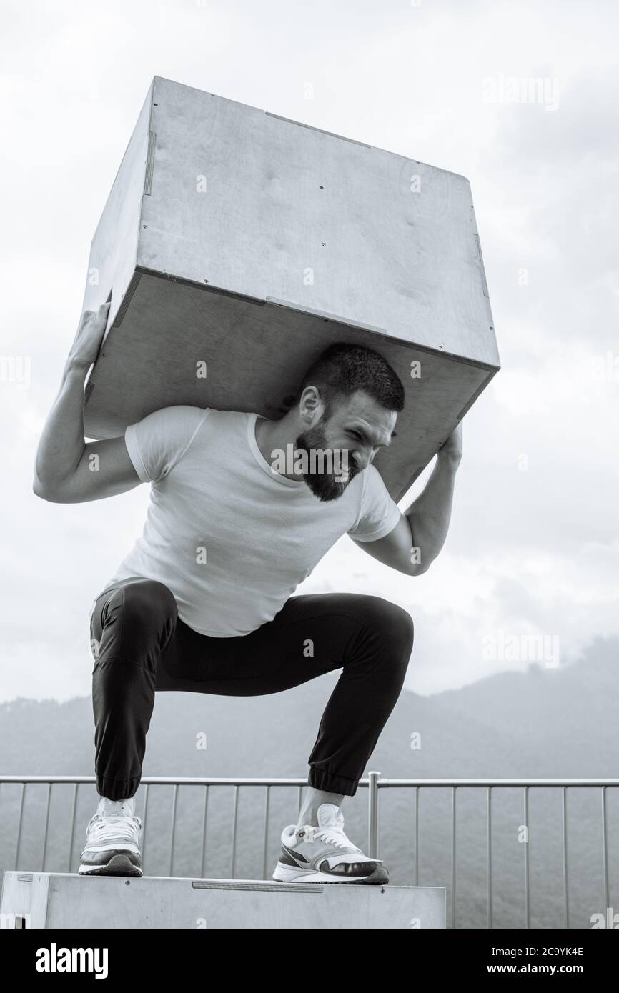 Young bearded athlete doing squats with weightning blocks over mountain ...