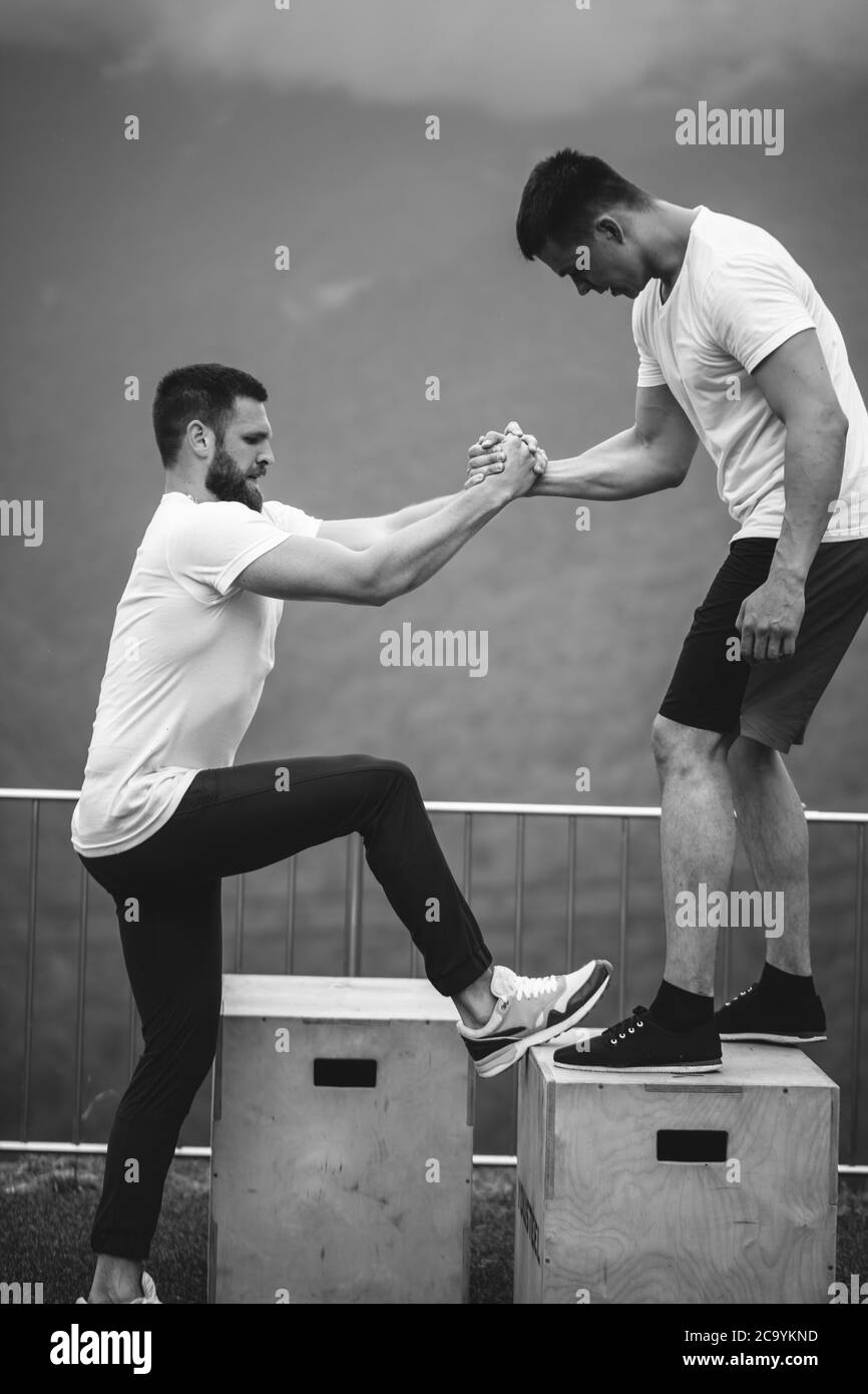 Two muscular athletes training, one raise the bar when other is ...