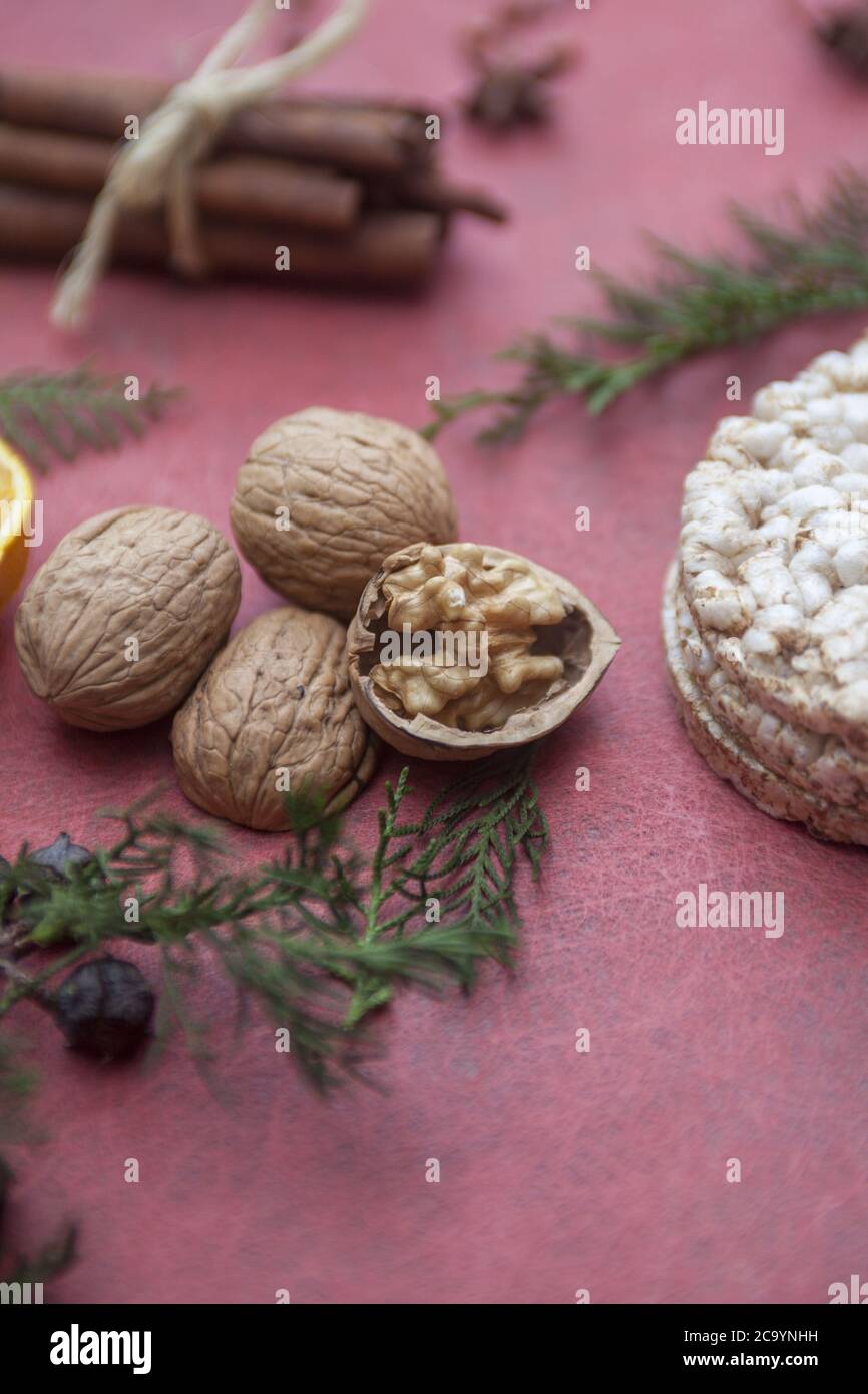 Vertical shot of walnuts, cinnamon sticks, and pine leaves on a red ...