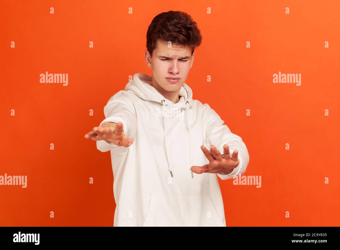 Young man in casual style hoodie standing with closed eyes and forward ...