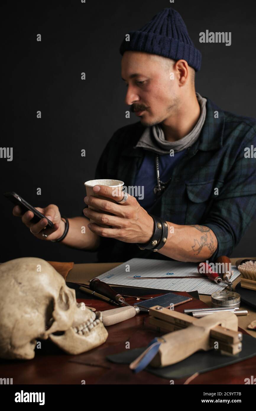 Cobbler Man using smart phone and holding cup of coffee in front of ...