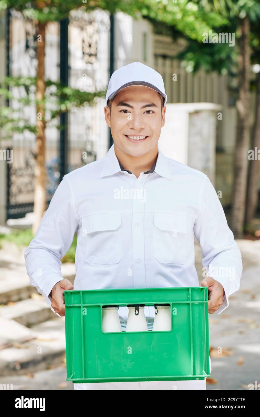 Portrait of happy handsome Vietnamese milkman carrying green plastic ...