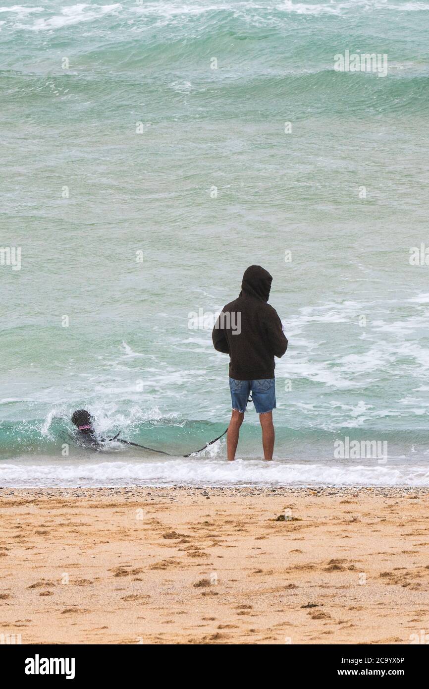 A holidaymaker wearing a hoodie and walking his dog along the shoreline ...