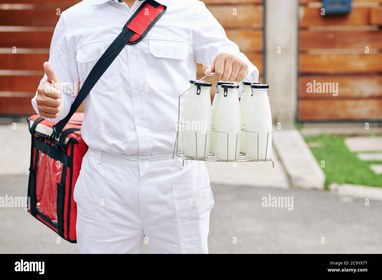 Cropped image of delivery man holding wire crate with glass milk ...