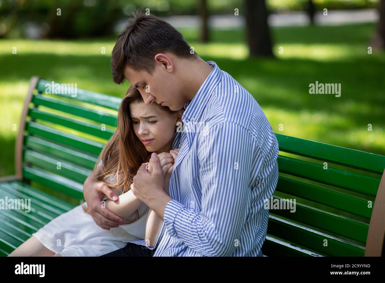 Young guy consoling his upset girlfriend on bench at park Stock Photo ...