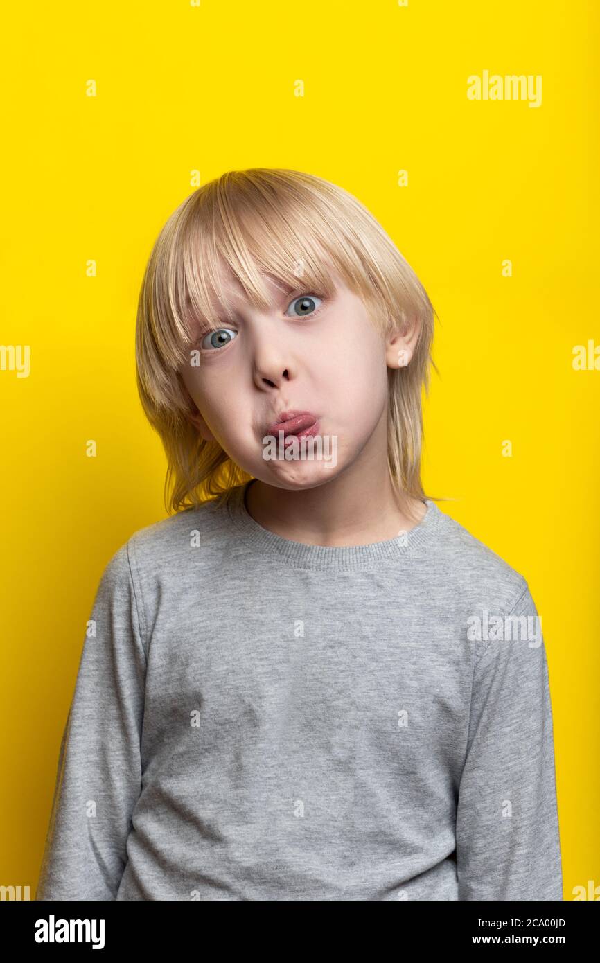 Funny fair-haired boy shows tongue and makes grimace. Vertical frame ...