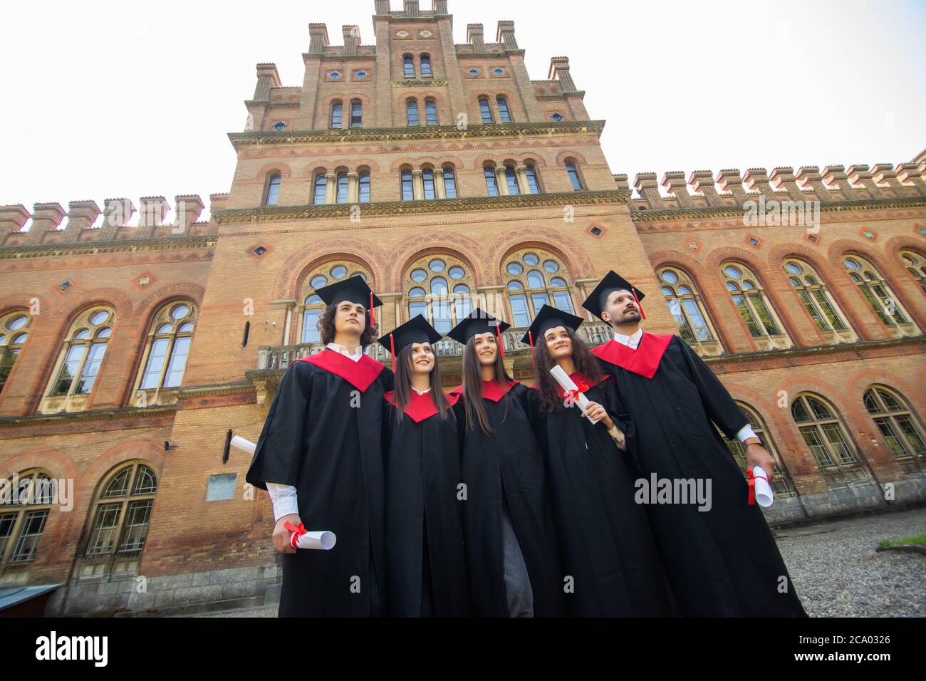 Happy graduates. Five college graduates standing in a row and smiling ...