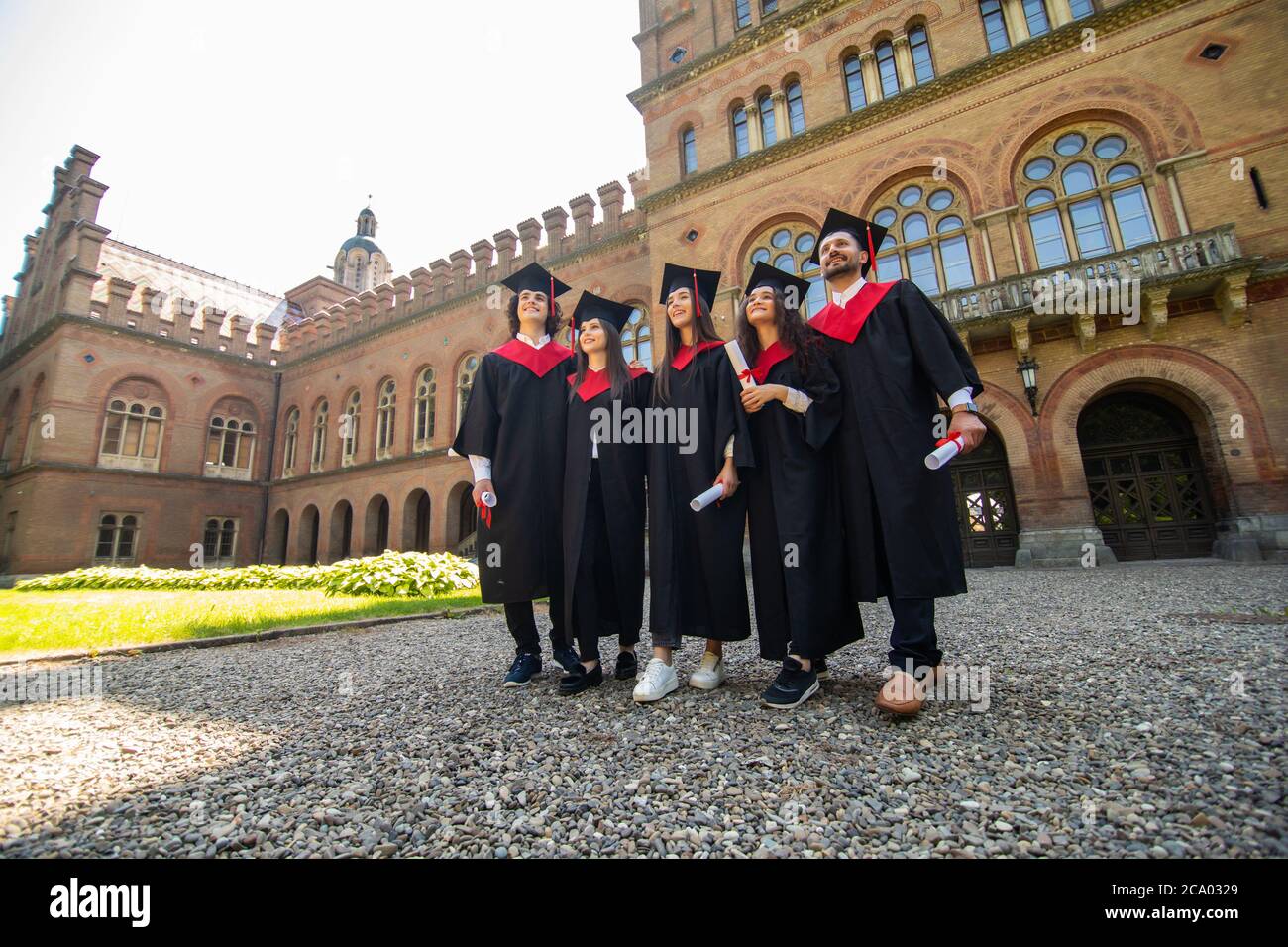 Happy graduates. Five college graduates standing in a row and smiling ...