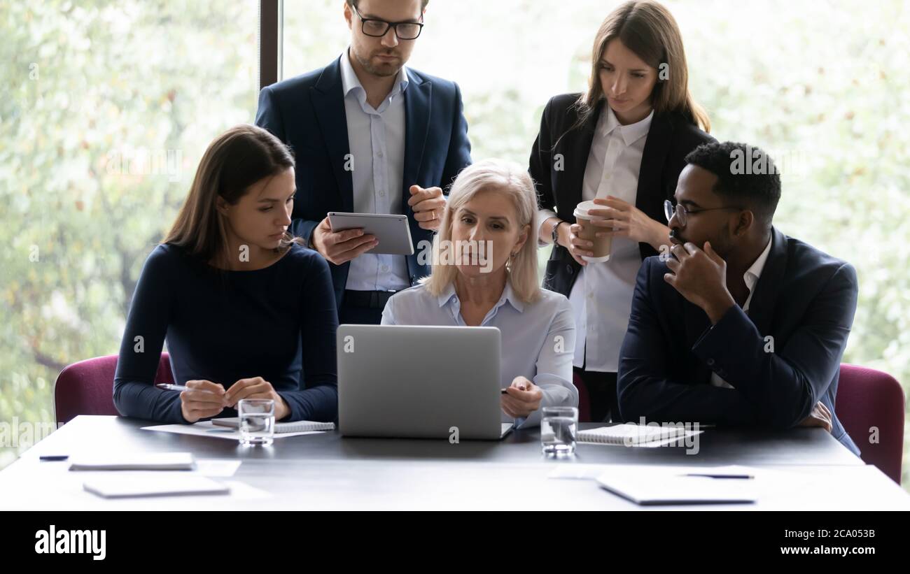 Middle-aged mentor teach young multiethnic employees using computer ...