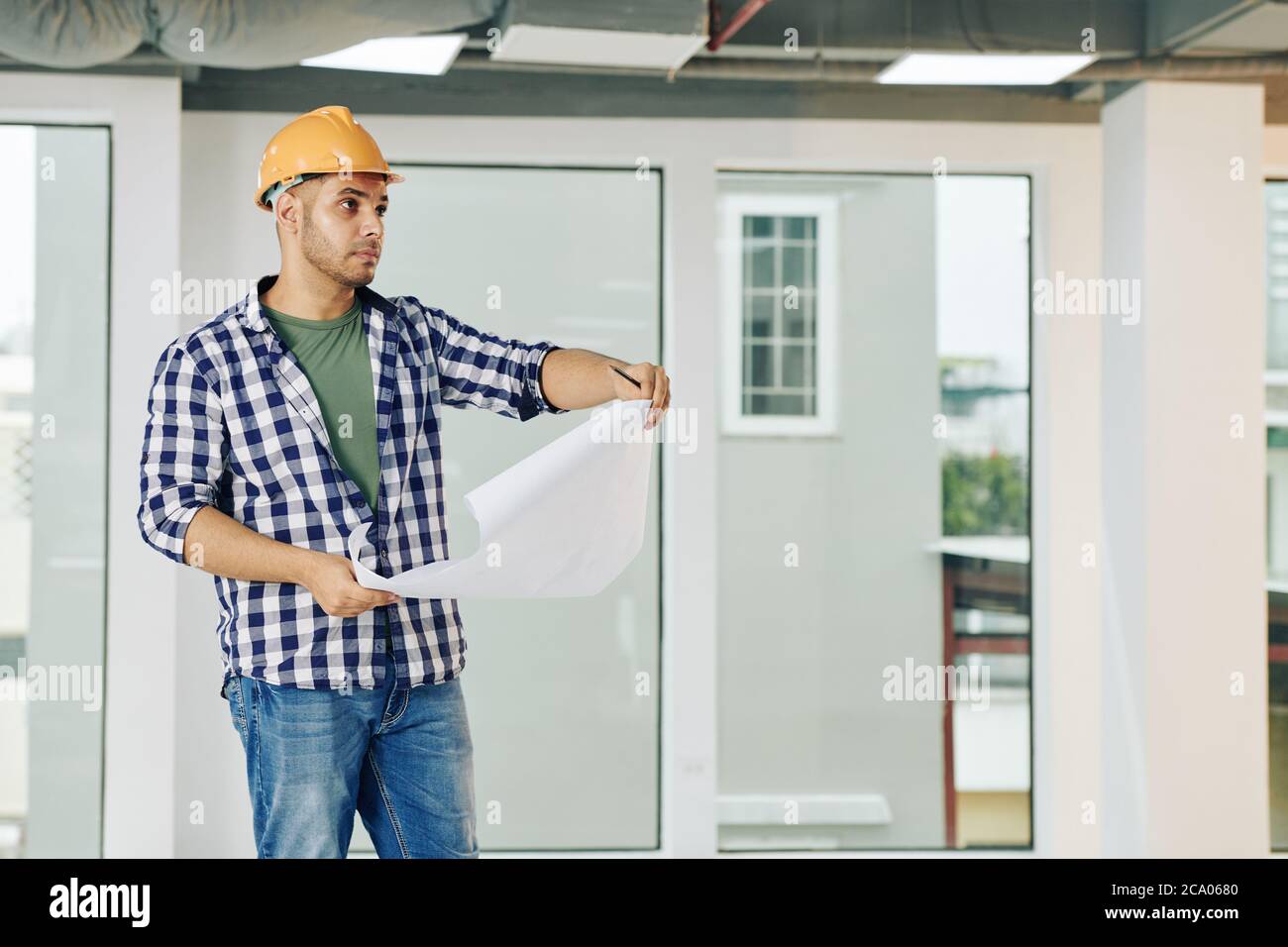 Serious handsome young construction engineer with blueprint checking ...