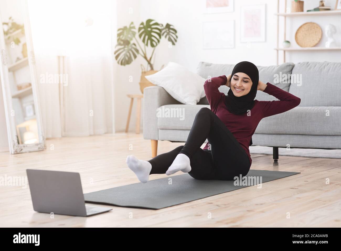 Sporty arabic woman in hijab doing abs exercises with laptop at home ...