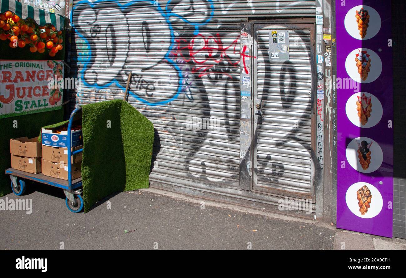 Metallic shop shutter, covered in graffiti, next to an outdoor stall ...