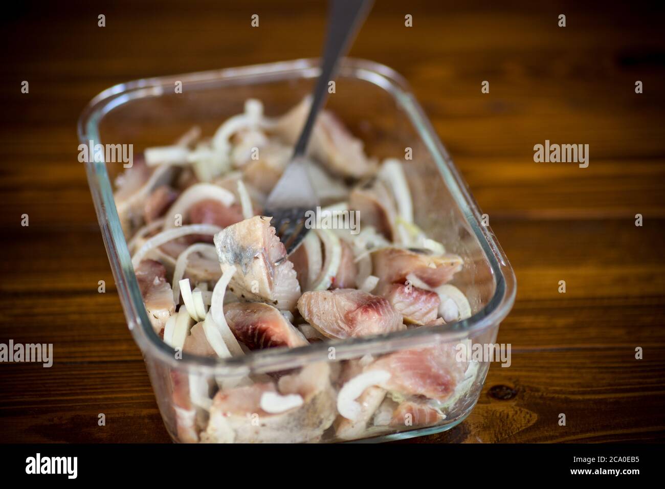 homemade salted herring pieces with onions and spices, on a wooden ...