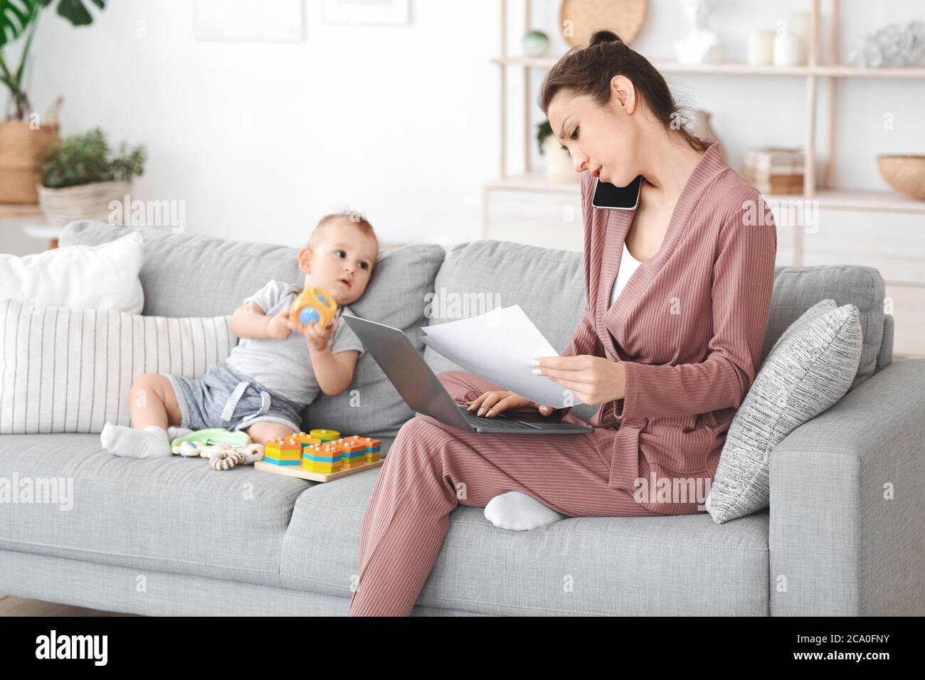 Mother working at home with laptop and papers next to her baby Stock ...