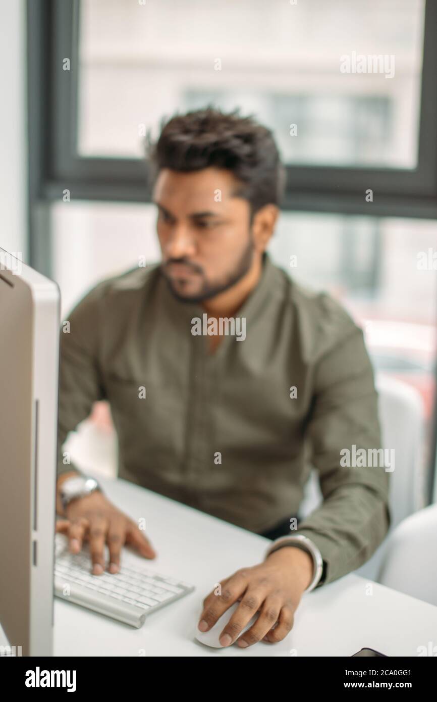 young indian man working at computer from modern bright office. focus ...