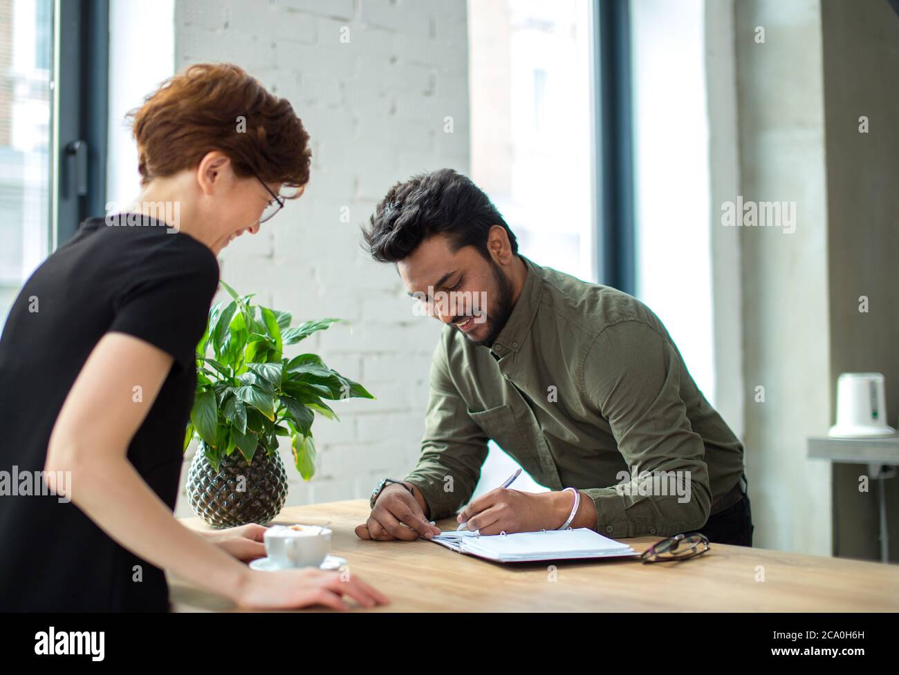 Two business people discuss meeting at table with documents and write ...