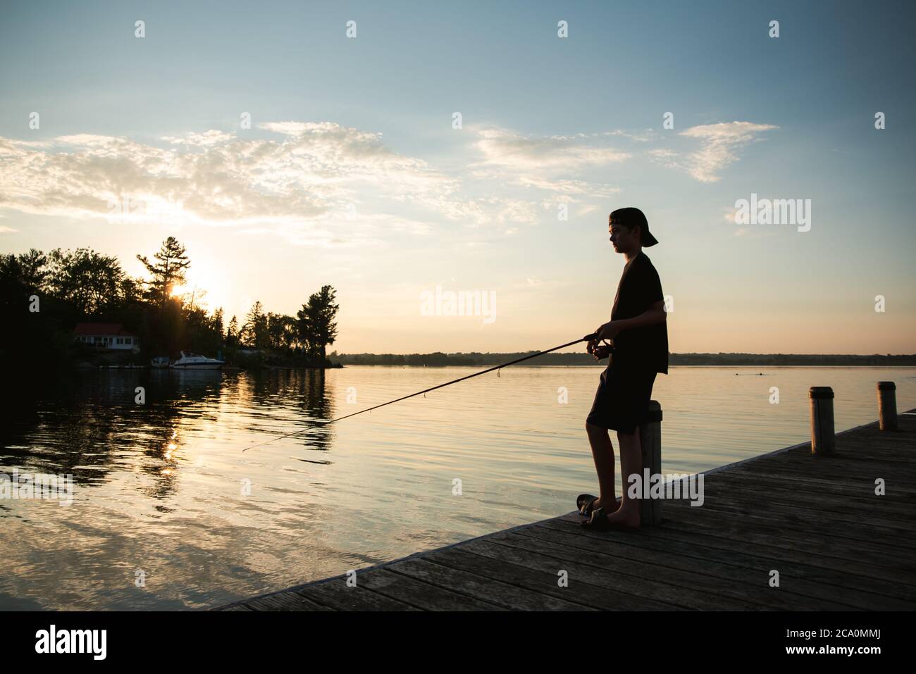 Adolescent boy fishing off dock on lake at sunset in Ontario, Canada ...