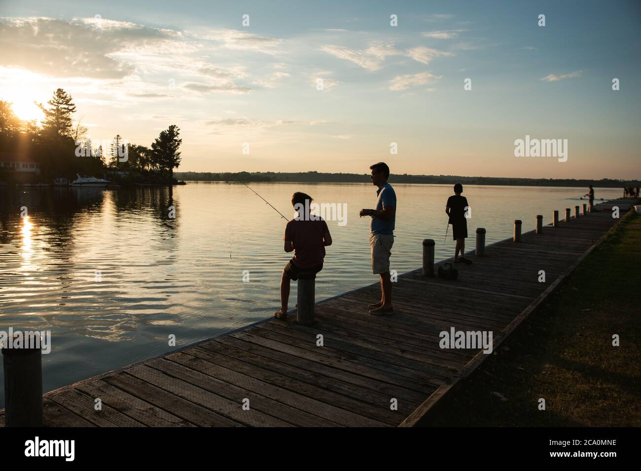Father and sons fishing on dock of lake at sunset in Ontario, Canada ...