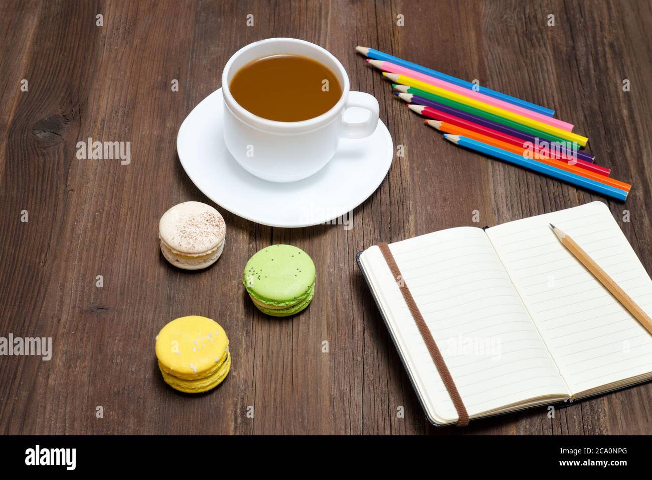 Coffee mug, macaroons, colored pencils and a notebook on a wooden ...