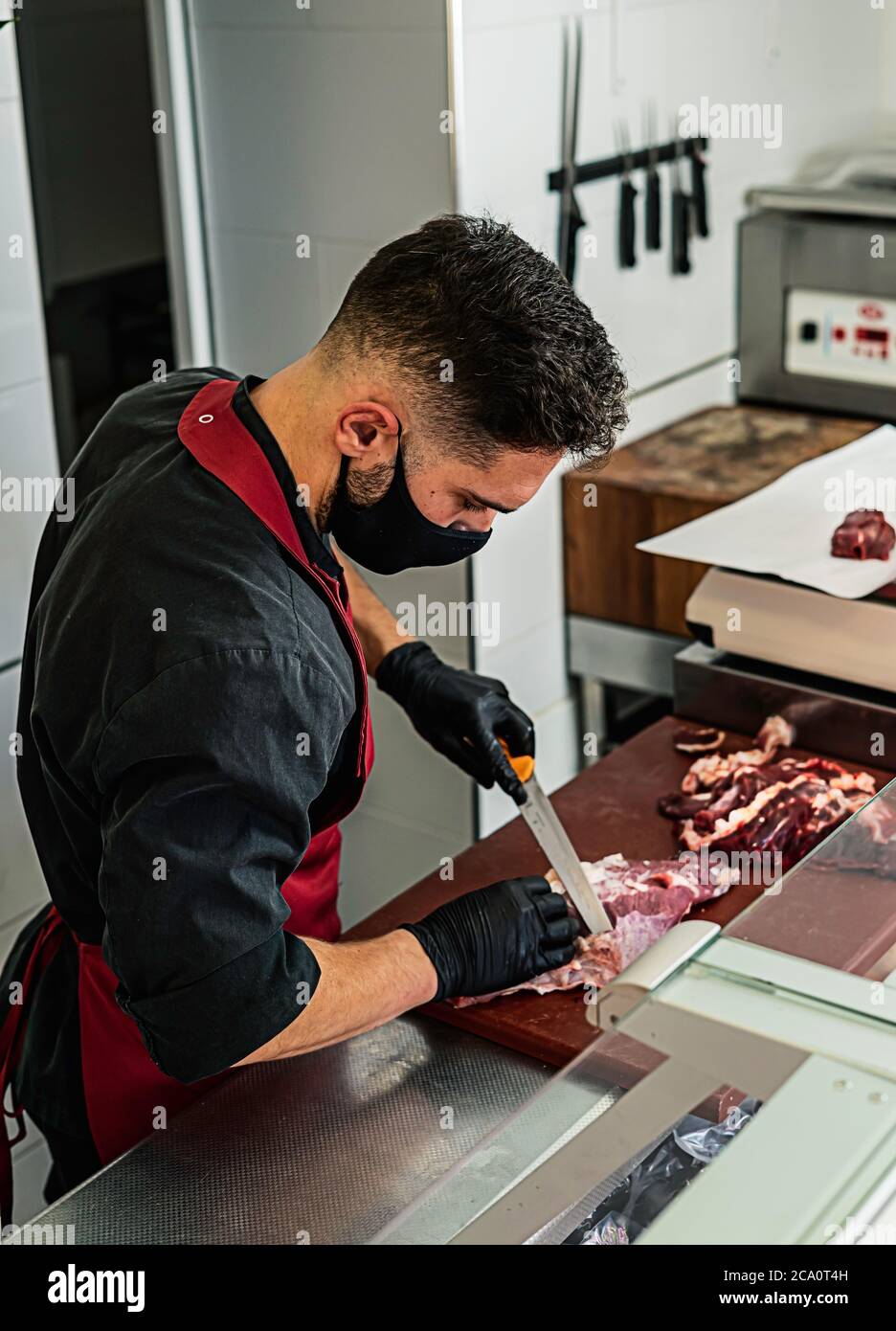 Professional butcher with mask cutting raw meat Stock Photo - Alamy