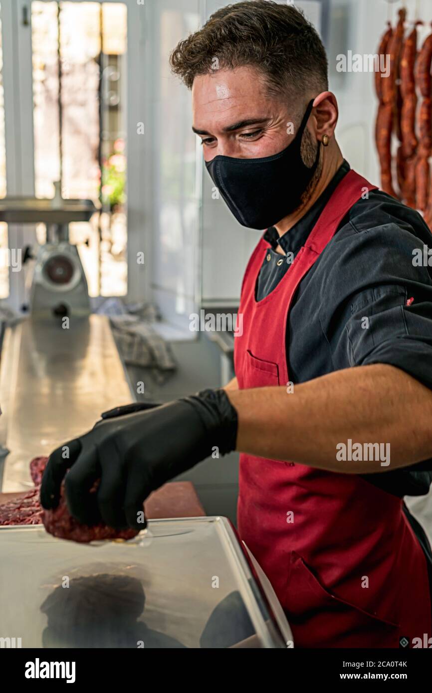butcher with mask making raw beef burgers in Butchers shop Stock Photo ...