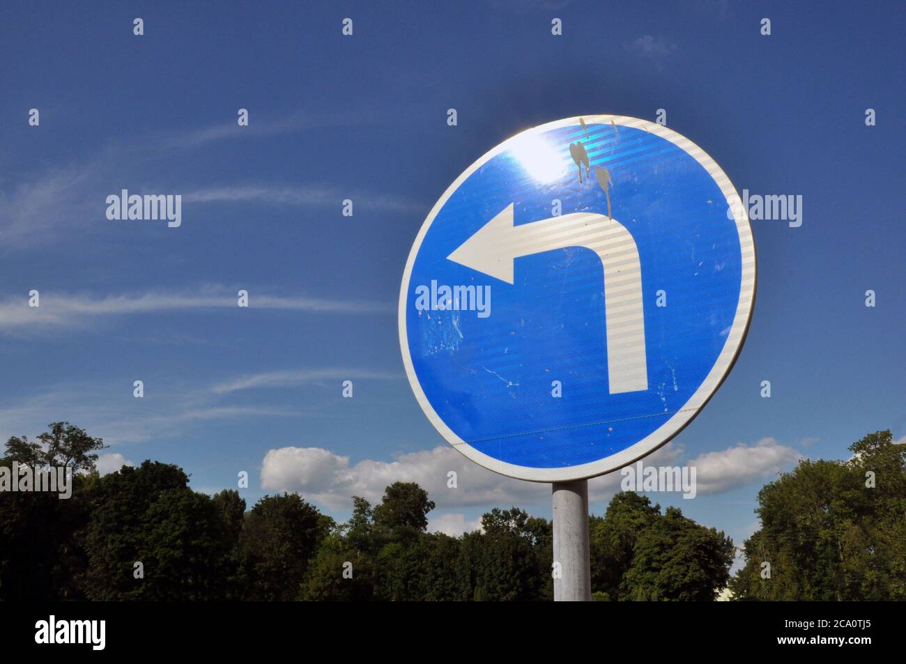 Road sign showing left turn against blue sky Stock Photo - Alamy