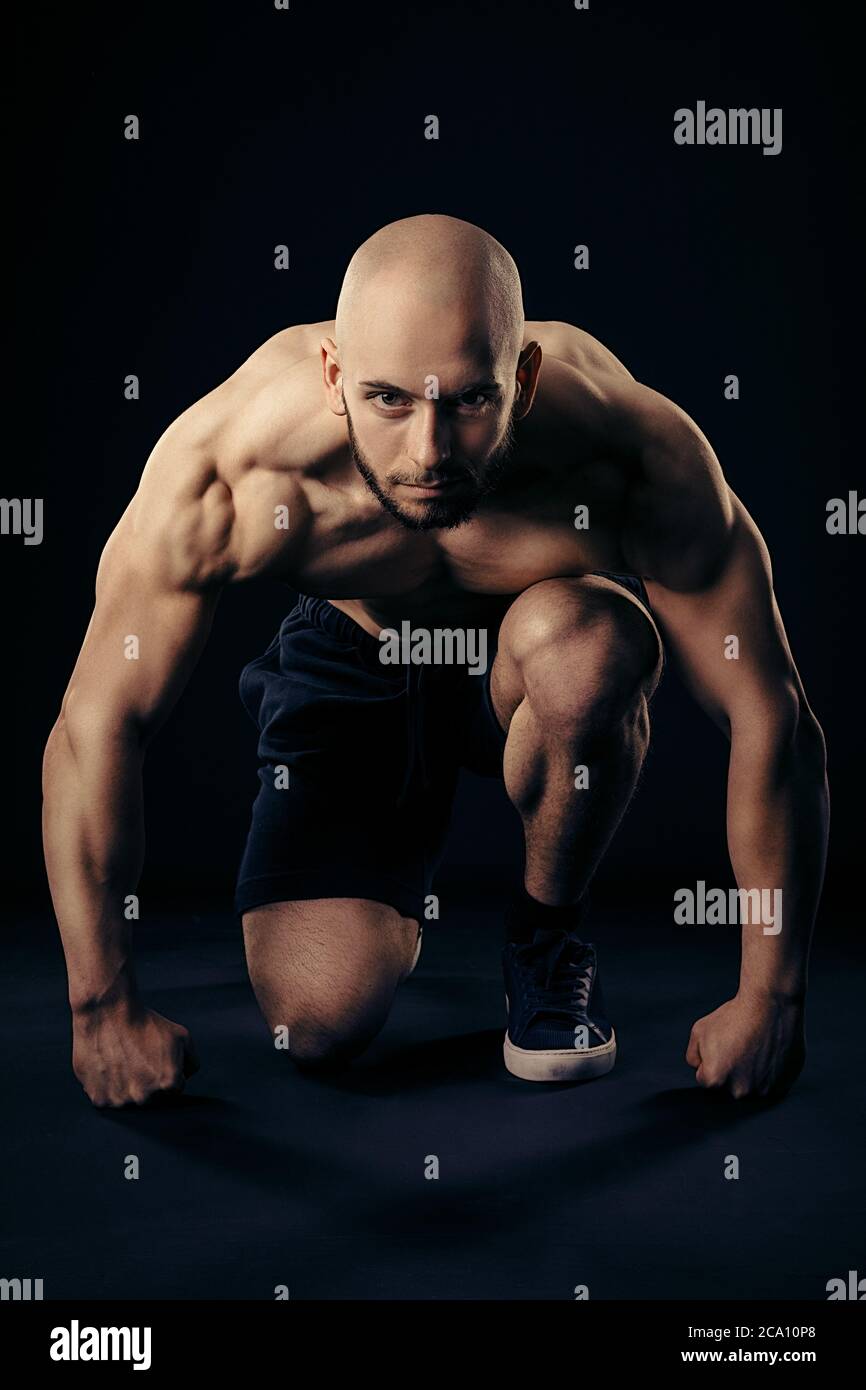 sportive muscular man crouching isolated on black background with ...