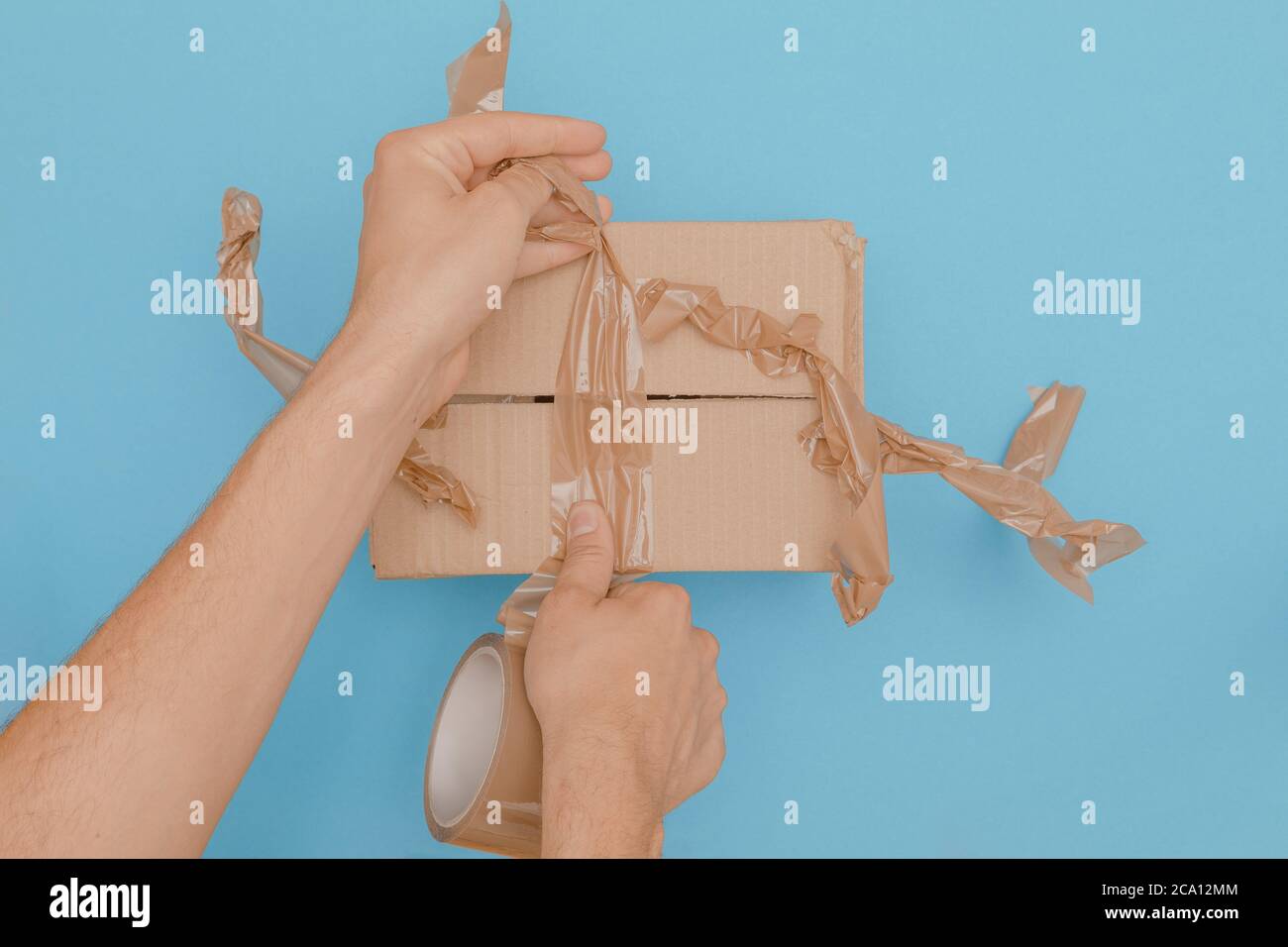 human hands try to wrap up a cardboard box with parcel tape to shut but ...