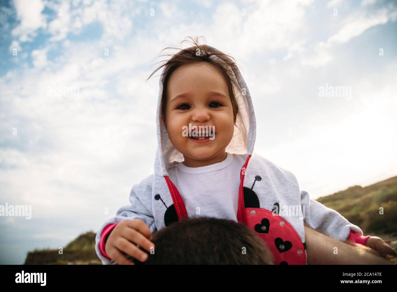 Close up of happy small baby girl in hood sitting on father's shoulders ...