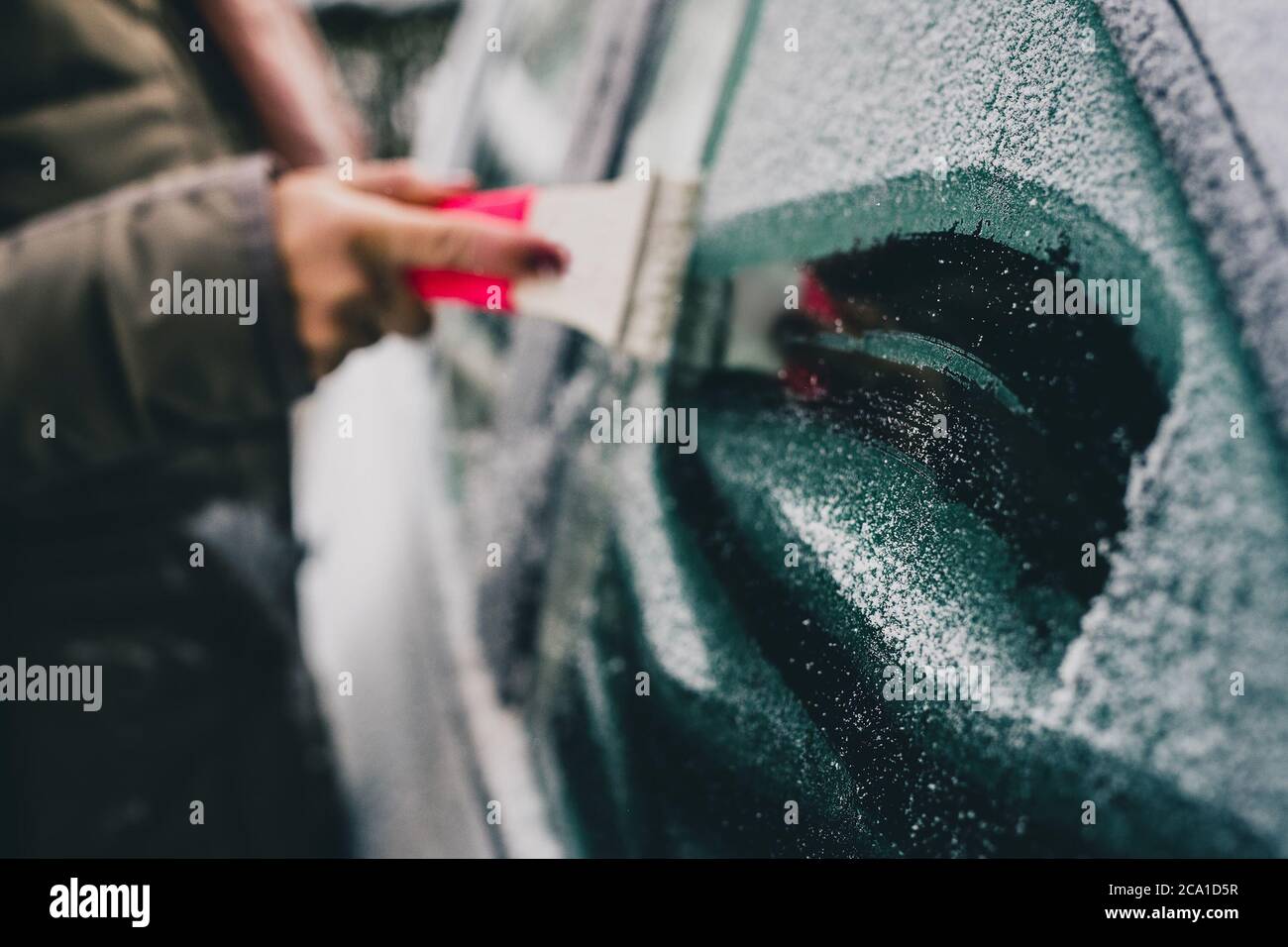 A woman is cleaning an icy window on a car with ice scraper. Focus on ...