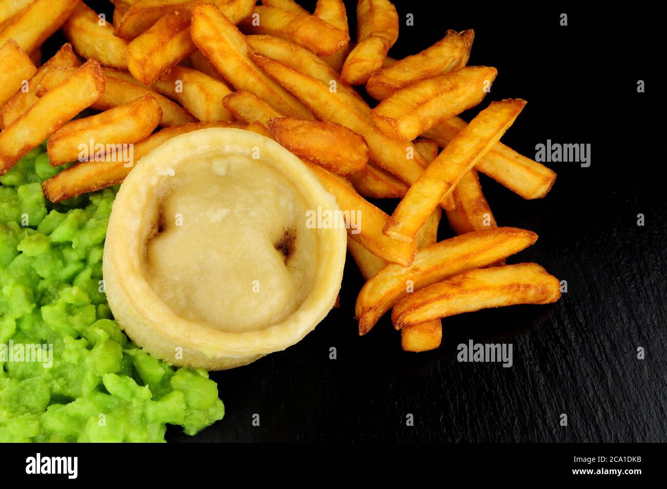 Steak and kidney pudding and chips meal with mushy peas meal on a slate ...