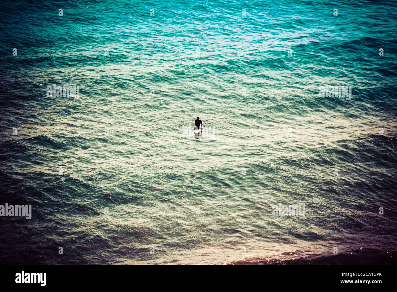 Elevated and Rear view of a lone surfer in Silhouette, sitting on ...