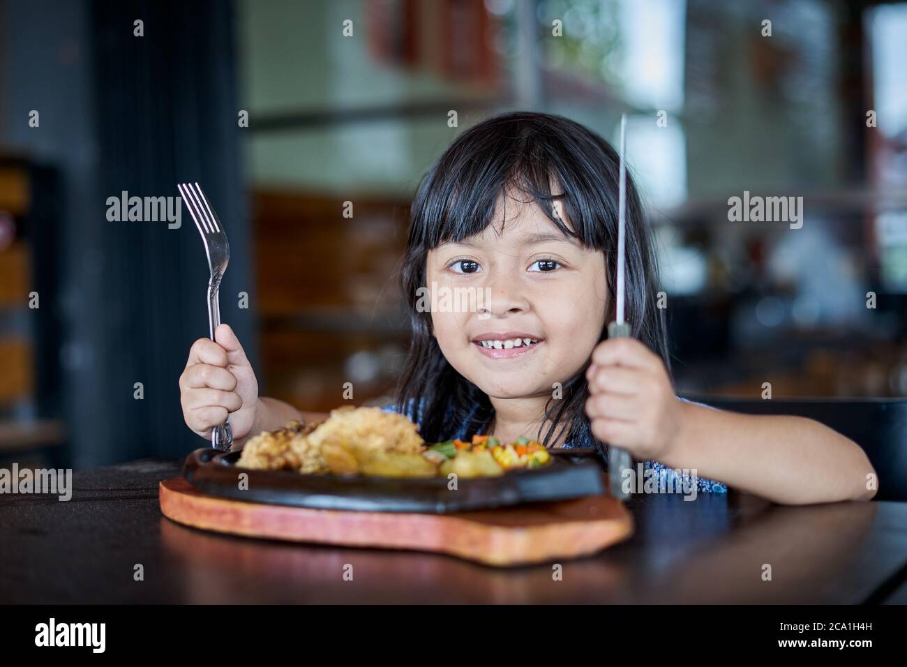 Happy little girl eating steak at local restaurant Stock Photo - Alamy