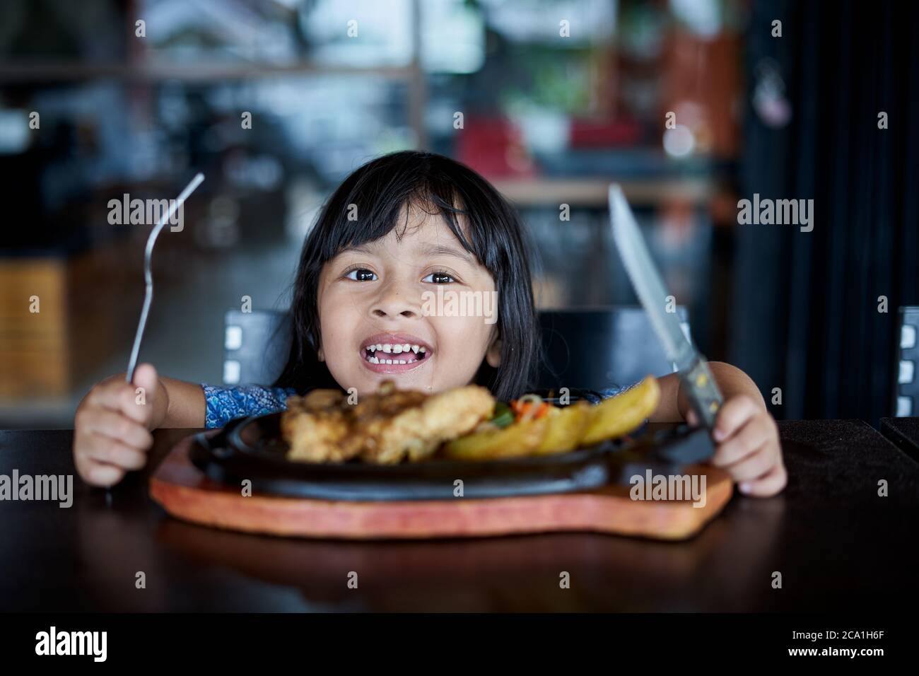 Happy little girl eating steak at local restaurant Stock Photo - Alamy