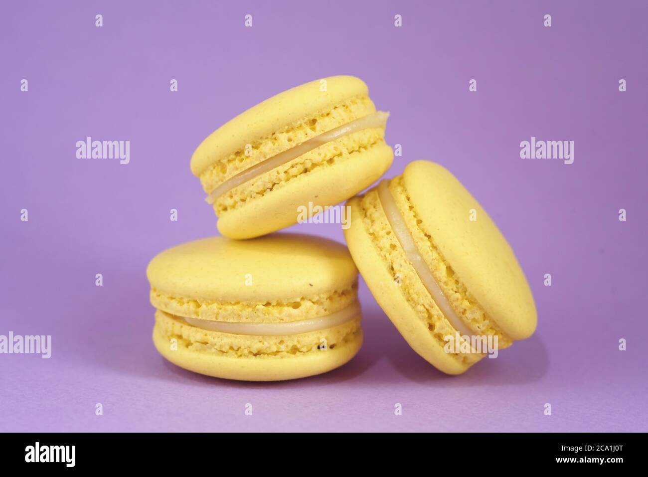 Three tasty french yellow colored macarons on the purple background ...