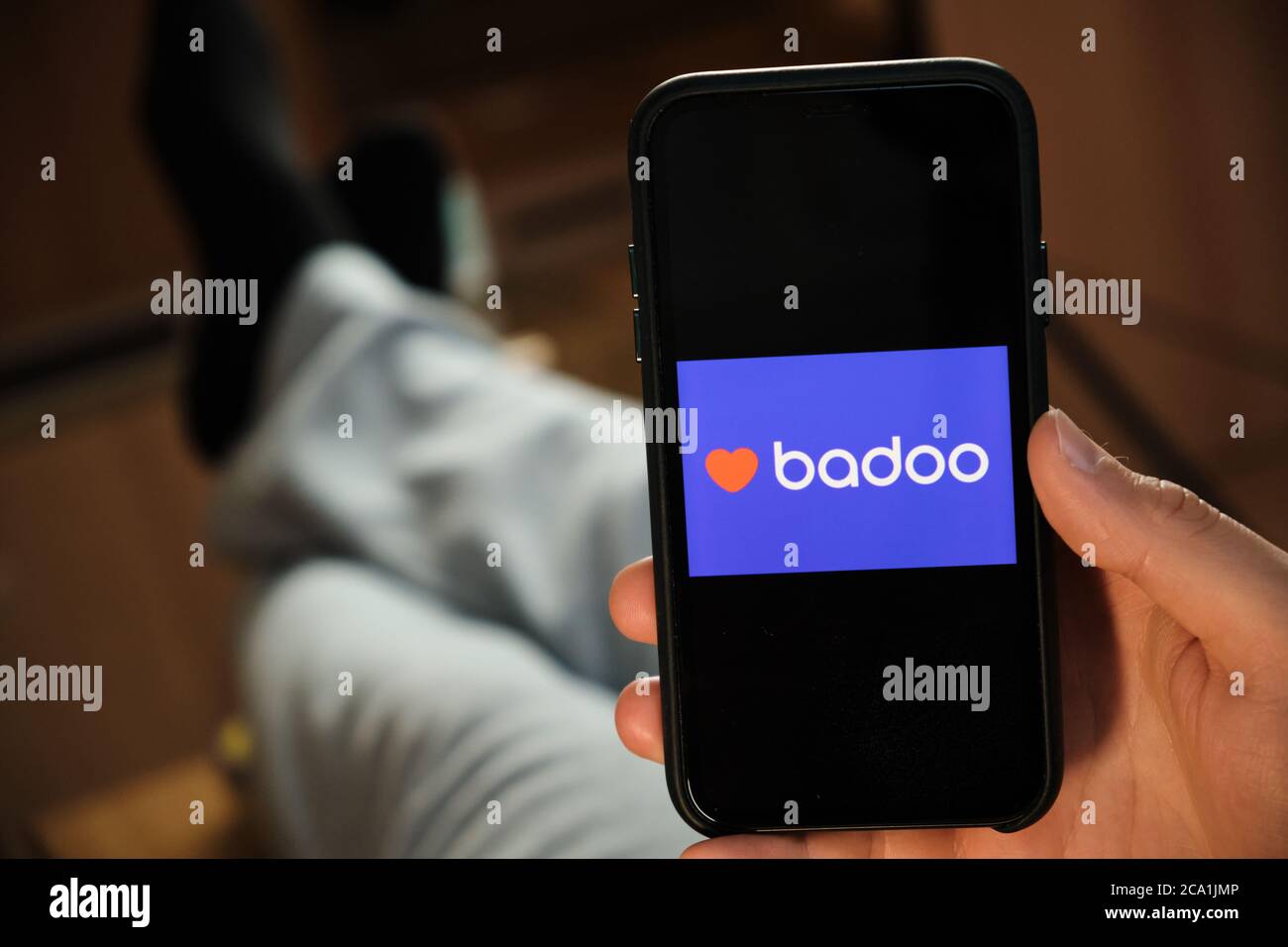 Badoo application on the smartphone in mans hand. Man laying and using ...