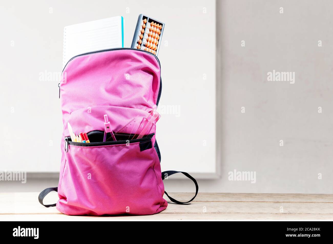 Backpack with book and stationary on wooden table with a whiteboard ...