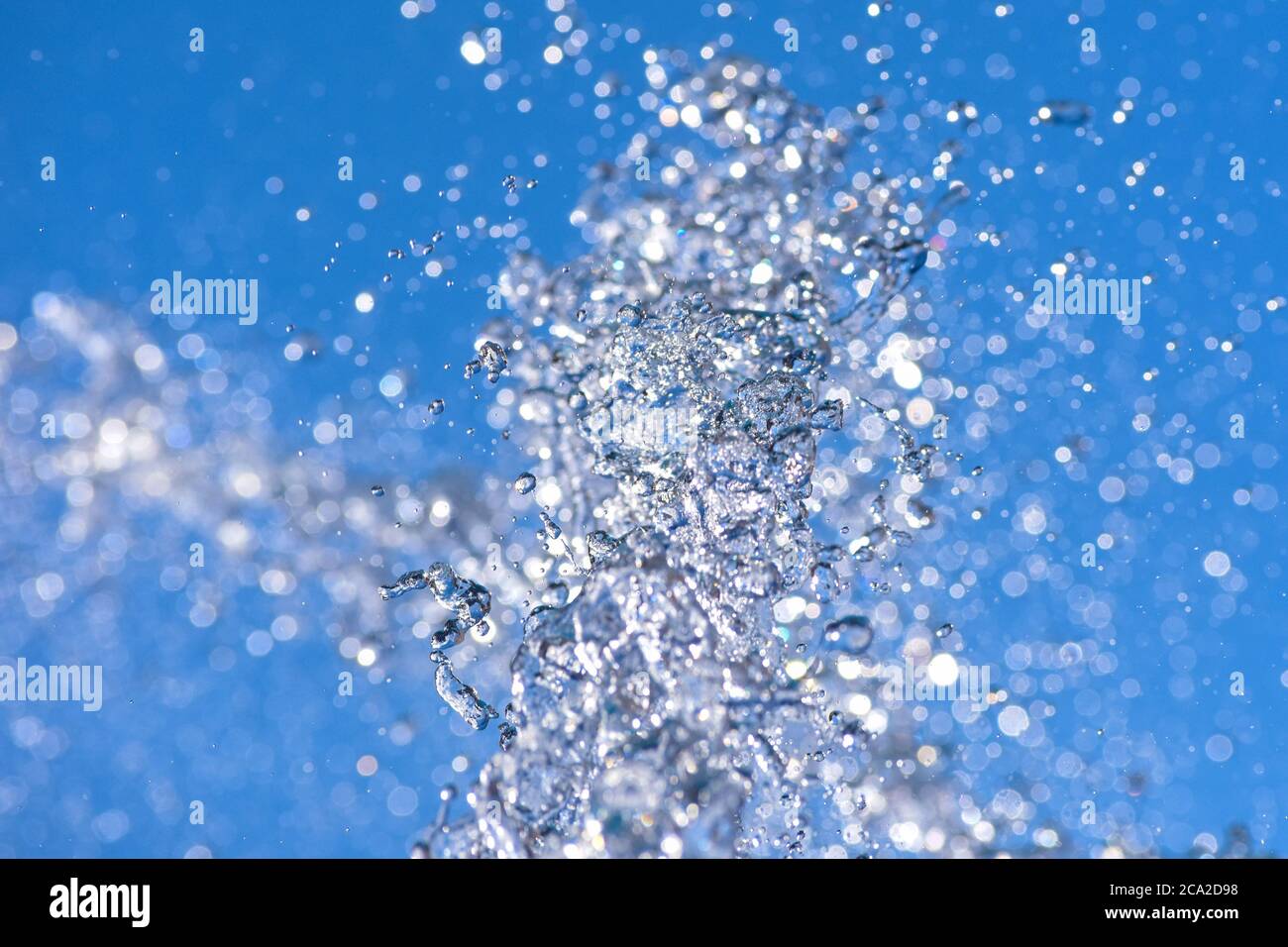 Water droplets spraying from a fountain in abstract design on blue sky ...