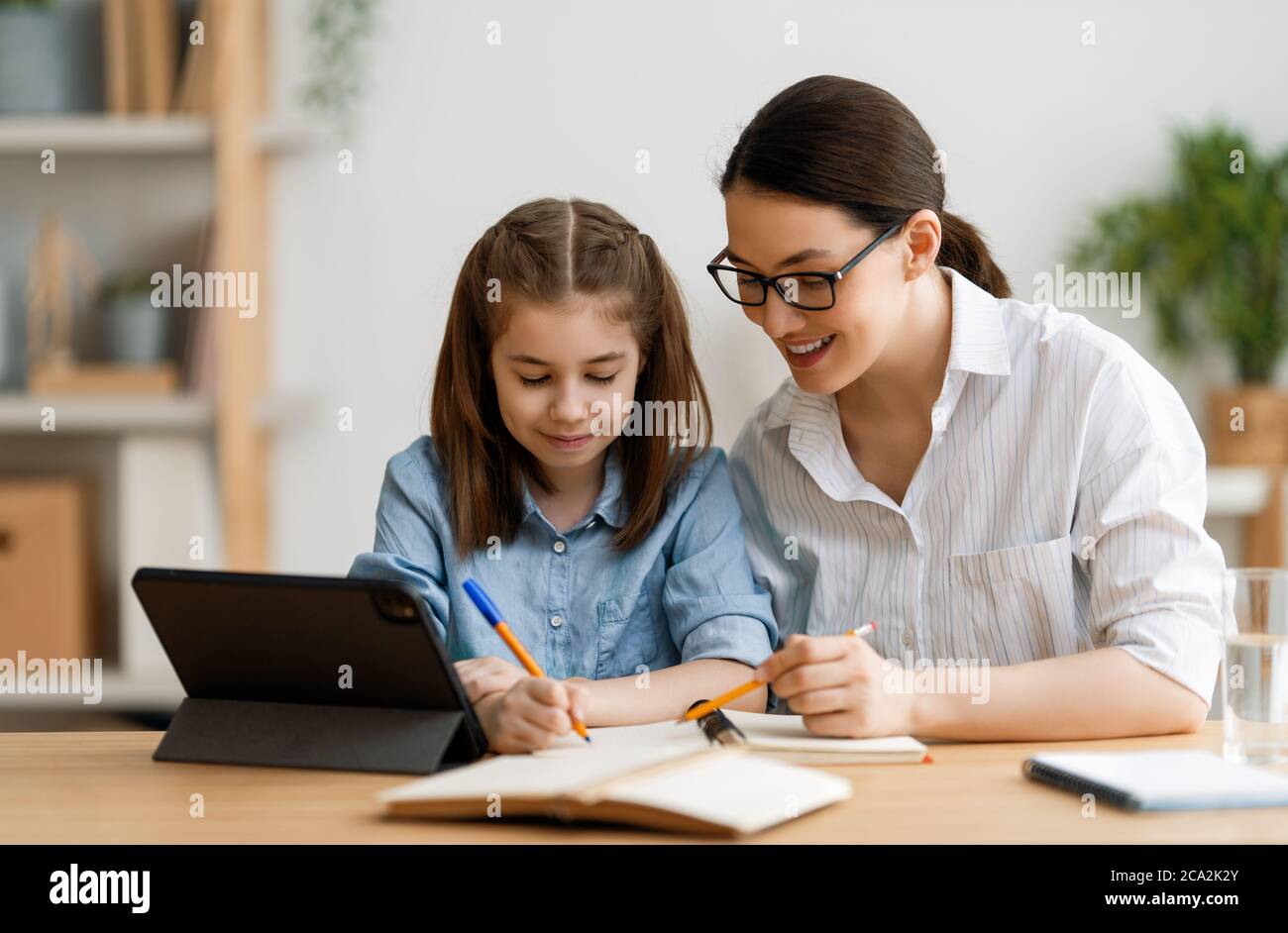 Back to school. Happy child and adult are sitting at desk. Girl doing ...